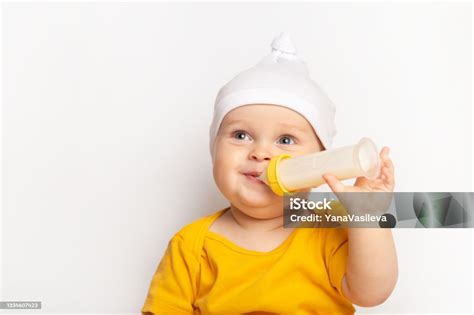 노란색 티셔츠와 흰색 배경에 모자를 입은 귀여운 행복한 백인 아기 소년의 초상화 아이는 카피 스페이스와 병에서 우유를 마십니다 영양 및 건강 관리 개념 우유에 대한 스톡