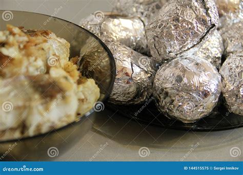 Slices Of Fried Fish In A Plate Next Baked Potatoes In Foil Stock