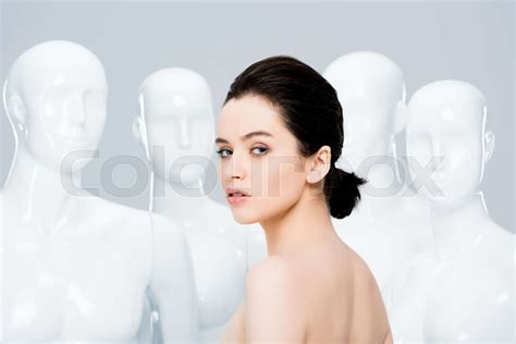 Beautiful Naked Girl Looking At Camera While Posing Near Mannequins Isolated On Grey Stock