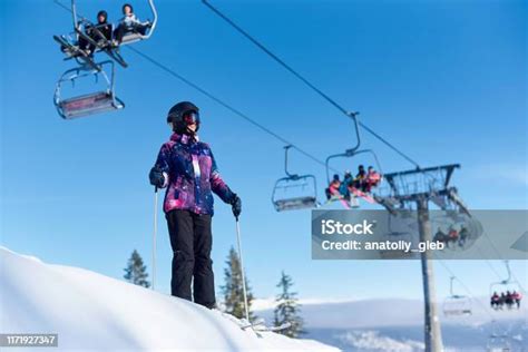 눈 덮인 산비탈에서 리프트 근처에 서있는 스키를 타는 행복한 여성 겨울 방학 동안 화창한 날 일반 보기입니다 겨울에 대한 스톡