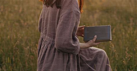 린넨 드레스를 입은 아름다운 여자가 일몰의 여름 초원에서 책을 손에 들고 걷고 있다 분위기 있는 차분한 순간 저녁 시골에서