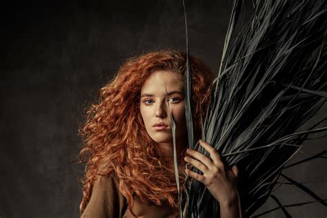 짙은 회색 배경에 키 큰 풀뭉치를 들고 있는 긴 물결 모양의 빨간 머리를 가진 아름다운 소녀 자연과의 연결 유기농 스킨케어 제품 광고 친환경 화장품 헤어케어 피부에 대한