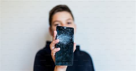 깨진 유리 화면 스마트폰이 화가 난 소년 흰색 배경의 손에 있습니다 집에서 깨진 스마트폰을 들고 걱정하는 아이 사진