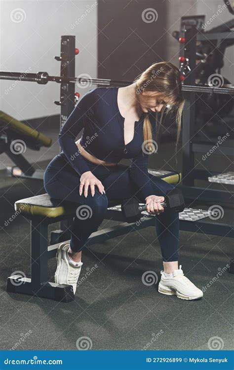 Woman Doing Biceps Curl With Dumbbells In Seated Position Wearing Blue Leggins And Long Sleeve