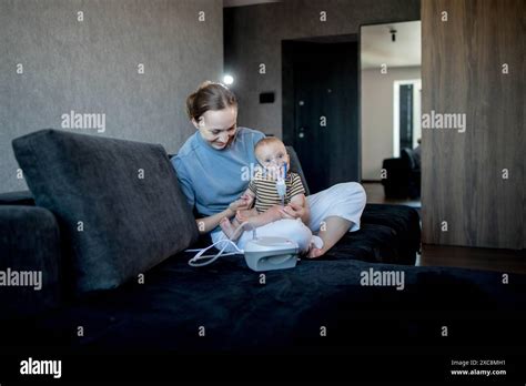 Woman With Infant Son Makes Inhalations Using A Nebulizer At Home Stock