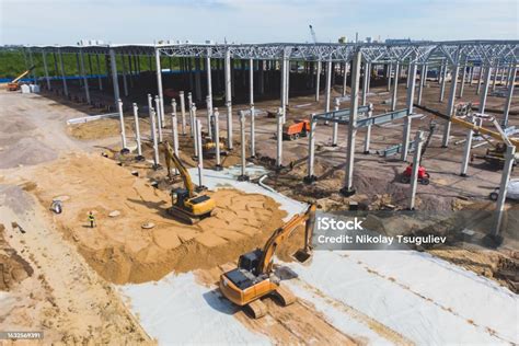 대형 창고 창고 건물 및 물류 센터 건설 현장 중장비 작업 굴삭기 크레인 트럭 및 불도저 현대 공장 격납고의 철골 구조 조감도 증기 롤러에 대한 스톡 사진 및 기타 이미지