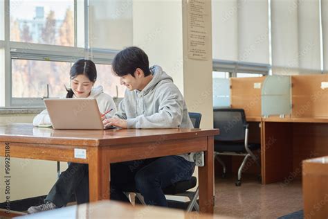 아시아 한국의 창밖의 가을 풍경과 도서관 책상에 앉아서 노트북을 보며 강의를 듣거나 공부를 하는 젊은 남녀 대학생 커플 모델