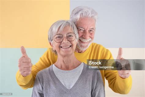 카메라를 보고 고립 된 다채로운 배경 위에 서 성숙한 미소 백인 노인 부부의 초상화 노인 흰 머리 사람들은 평온한 미소 손으로 제스처를 행복한 엄지 손가락을하고 수염 남자