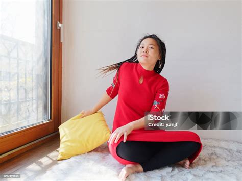 햇살 집에 귀여운 험 상와 젊은 중국 여자의 모피 카펫 노란 쿠션 들고와 멋진 표정으로 카메라를 보고 앉아 흰색 벽 배경과 격리 땋은 머리에 대한 스톡 사진 및 기타 이미지