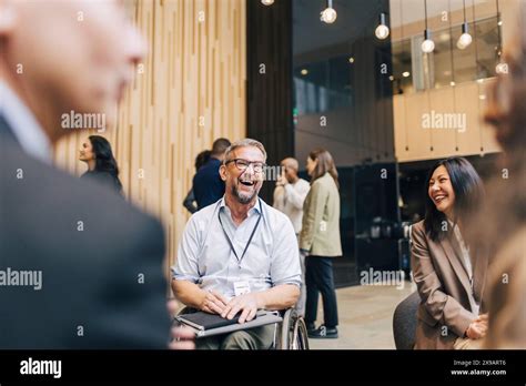 Happy Mature Businessman With Disability Sitting On Wheelchair While Discussing With Delegates