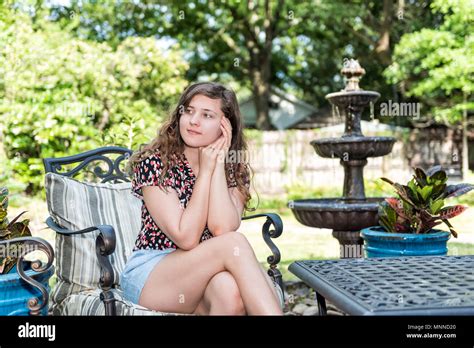 Young Woman Sitting On Patio Chair In Outdoor Spring Garden In Backyard