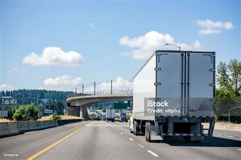 다른 교통 뒤의 넓은 고속도로 도로에서 달리는 드라이 밴 세미 트레일러에서 화물을 운반하는 큰 장비 흰색 세미 트럭 호송에 대한 스톡 사진 및 기타 이미지 Istock