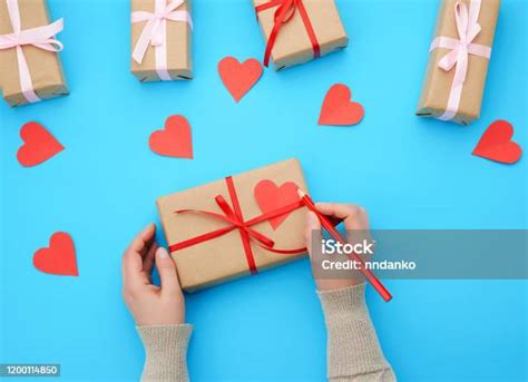 여성의 손은 갈색 크래프트 종이에 싸여 파란색 배경에 실크 리본으로 묶여 상자를 보유하고 갈색에 대한 스톡 사진 및 기타 이미지