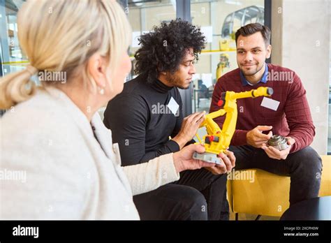 Group Of Professionals Discussing Robotics And Automation Using A Model Robotic Arm Concept Of