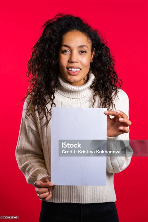 흰색 A4 종이 포스터를 들고 아프리카 머리와 예쁜 혼합 인종 소녀 공간을 복사합니다 빨간 스튜디오 배경에 트렌디 한 여자를