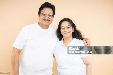비행기 흰색 티셔츠를 입은 행복한 인도 노부부의 초상화는 베이지색 스튜디오 배경에 고립되어 서 있다 카메라를 보고 있는 아시아 성숙한 남자와 여자 T 셔츠에 대한 스톡 사진
