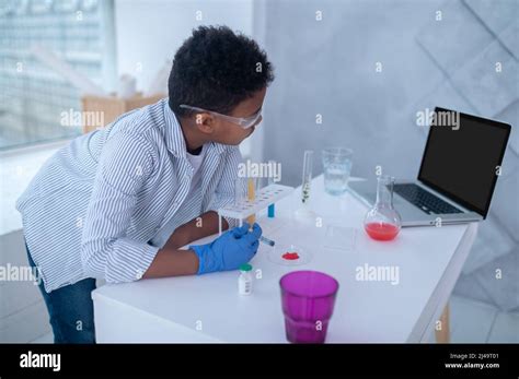 A Dark Haired Boy In A Lab Coat Looking Busy While Doing Chemical