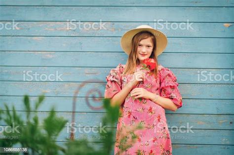 귀여운 소녀 레드 스트라이프 드레스 밀 짚 모자를 쓰고 장미 꽃을 들고 밝은 파란색 나무 배경에 포즈의 여름 가족에 대한 스톡 사진 및 기타 이미지 Istock