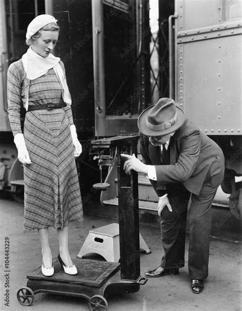 Profile Of A Man Measuring Weight Of A Woman Standing On A Weighing Scale In Front Of A Train