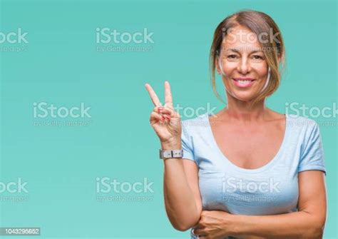 중간 나이 승리 표시를 하 고 카메라에 윙크 하는 행복 한 얼굴로 웃 고 고립 된 배경 위에 수석 히스패닉 여자 번호 2입니다 긍정적인 감정 표현에 대한 스톡 사진 및 기타