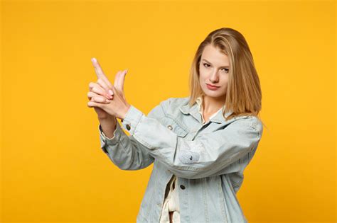 스튜디오에서 노란색 오렌지 벽 배경에 고립 된 총 처럼 손을 잡고 카메라를 찾고 데님 캐주얼 옷에 자신감 젊은 여자의 초상화 사람들 라이프 스타일 개념입니다 복사 공간을