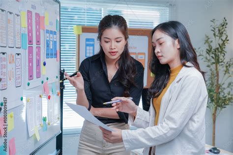 Two Asian Ui Ux Designers Are Working Together In The Office Discussing Over Mobile App