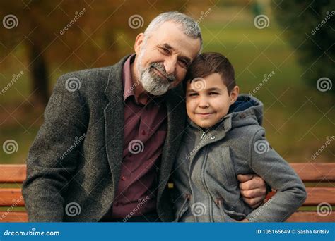 Grandpa And His Grandson Spend Time Together In The Park They Are Sitting On The Bench Stock