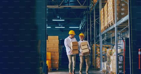 흰색 유니폼을 입고 머리에 노란색 헬멧을 쓴 두 명의 블루 칼라 노동자가 창고에서 무거운 상자를 옮깁니다 사진 Unsplash의 네덜란드 이미지