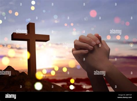 Christian Cross And Male Hands With Praying Position Over Sunset