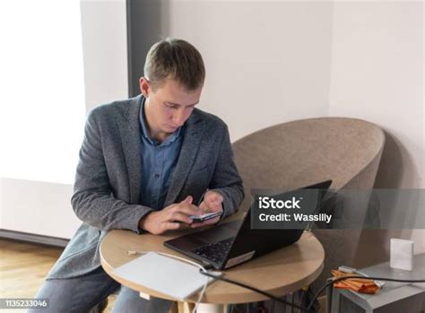 동료에 게 문자 메시지 스마트 캐주얼 착용에 자신감 젊은 남자 사무실에서 그의 작업 장소에 앉아 있는 동안 그것을 보고 스마트폰