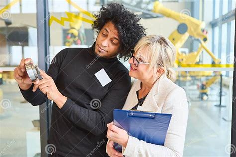 Engineers Discussing Robotics Component In Industrial Setting With Gripper Arms In Background