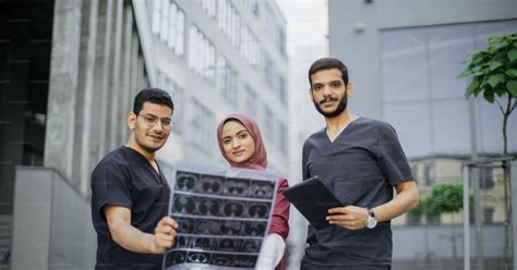 세 명의 의사 히잡을 쓴 여성과 의료용 의류를 입은 두 명의 남성이 환자의 엑스레이 단층 촬영 스캔에 대해 논의하고 현대 병원을 배경으로 밖에 걸어 나간다 사진