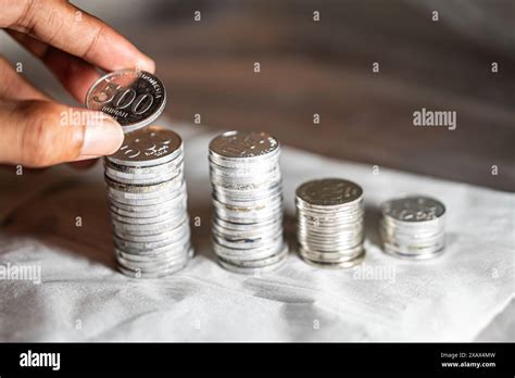 a person stacking silver coins in ascending order on a white surface