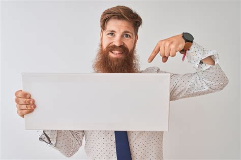 자신에게 손가락을 가리키는 깜짝 얼굴과 고립 된 흰색 배경 위에 서있는 배너를 들고 있는 젊은 빨간 머리 아일랜드 사람 가리키기에 대한 스톡 사진 및 기타 이미지 Istock