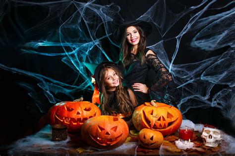 귀여운 어린 소녀와 마녀 모자에 아름다운 엄마는 카메라에보고 있는 동안 배경에 앉아 10월에 대한 스톡 사진 및 기타 이미지 10월 가을 가정 생활 Istock