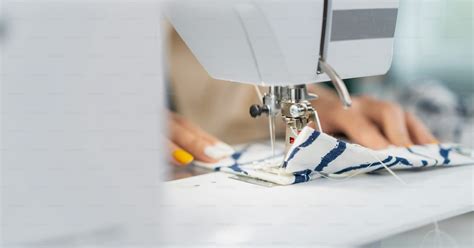 디자이너의 손을 닫으면 재봉틀에서 직물 소재를 밀어 넣습니다 아름다운 젊은 패션 재단사 여성이 작업실이나 재봉 아틀리에에서