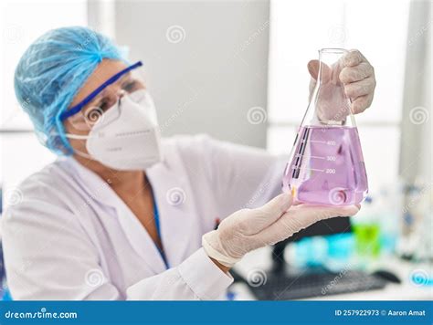 Middle Age Woman Wearing Scientist Unifor And Medical Mask Holding Test Tube At Laboratory Stock