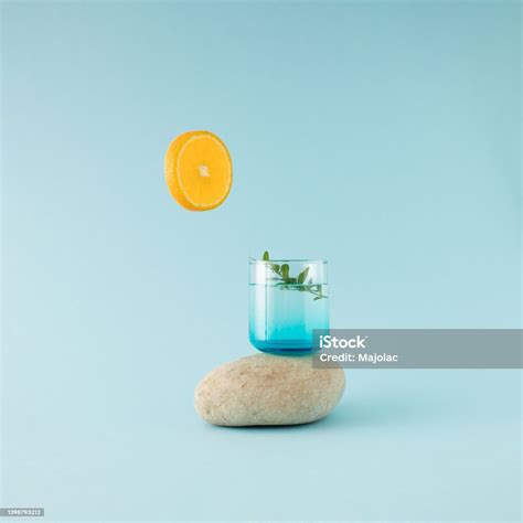 돌 위에 서있는 신선한 맑은 물로 가득 찬 음료 유리는 태양처럼 작용하는 오렌지색 조각으로 덮여 있습니다 최소한의 여름 개념 0명에 대한 스톡 사진 및 기타 이미지 Istock