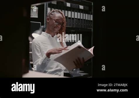 Detective Inspector Examining Case Files Information In Police Archive Room Reading Witness