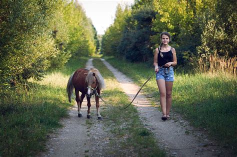 십대 소녀는 여름 저녁에 시골 비포장 도로를 따라 목줄에 조랑말 콜트를 들고 걷고 있습니다 8월에 대한 스톡 사진 및 기타 이미지 Istock