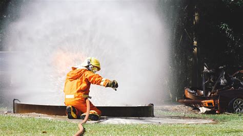 소방관은 화재 호스 화학 물 거품 스프레이 엔진을 사용하여 화염과 싸우고 소방관은 하드 모자 보호를위한 바디 안전 정장 유니폼을 착용합니다 소방 소화기 구조 훈련 건물