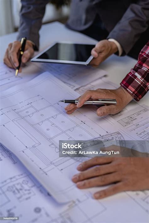 Engineering Team Meeting For Colleagues Discussing And Reviewing Blueprints At Desk In Office