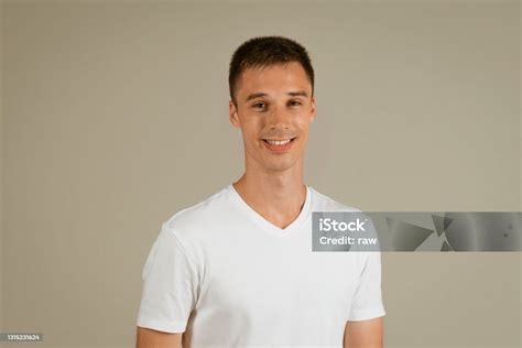 흰색 티셔츠를 입은 짧은 헤어스타일을 가진 젊고 어른스러운 검은 머리의 남자가 스튜디오에서 가벼운 배경을 가진 감정적으로 포즈를 취하고 있습니다 25 29세에 대한 스톡