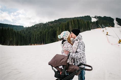 젊은 가족 커플 키스 카 르 파티 안 산에서 눈에 유모차 근처 숲과 리프트와 스키 슬로프의 배경에 닫습니다 겨울 자연 산에서 호 이스트 눈을 만드는 대포 겨울에 대한 스톡