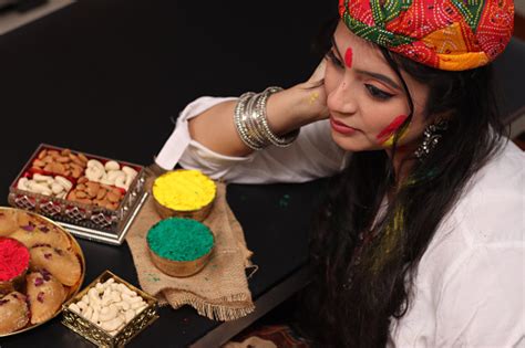 Holi 색상의 축제를 축하하기 위해 Abeer Gulal 드라이 컬러 파우더와 인도 달콤한 Gujiya Pedukiya Kashew를 준비하는 앉은 자세의 아름다운 여성