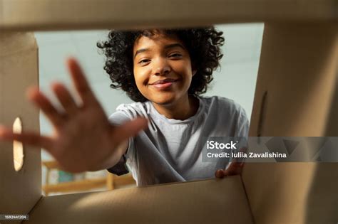 카드 상자 아래쪽 보기 내부 아프리카 소녀가 포장을 풀고 배달을 상자에 넣고 있습니다 판지 상자를 여는 여자 배달된 상품 품목을 보고 소포를 받는 여성 만족스러운 고객