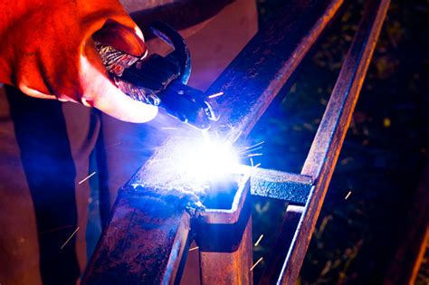 용접기 작업자가 점프 용접을 수행합니다 보호 장갑의 남자 용접기는 금속 구조의 아크 용접 공정을 수행합니다 용접 기에서 불꽃 비행 배경 건설 현장 강철에 대한 스톡 사진 및