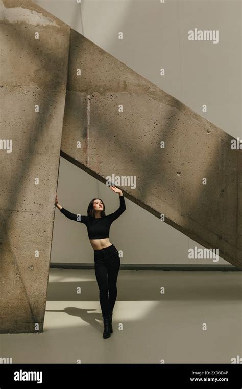 A Young Woman Poses In A Modern Urban Environment Under Angular Concrete Structures