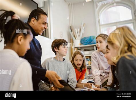 Male Teacher Sharing Tablet Pc With Students Discussing In Classroom