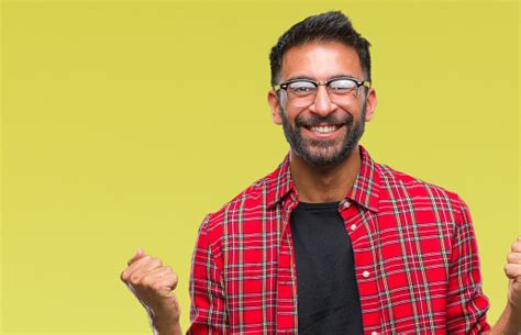 축 하 하는 고립 된 배경 위에 안경 착용의 히스패닉 남자 성인 개는 놀라게 하 고 무기와 성공을 위한 제기 및 오픈 눈 깜짝 놀라게 우승자 개념입니다 긍정적인 감정 표현에